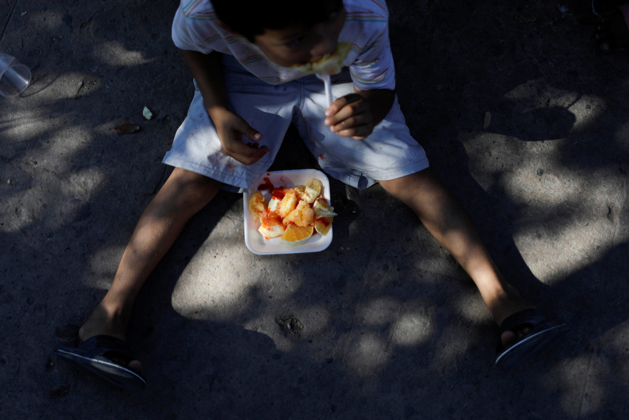A migrant boy seeking asylum into the U.S. eats orange as he waits with ...